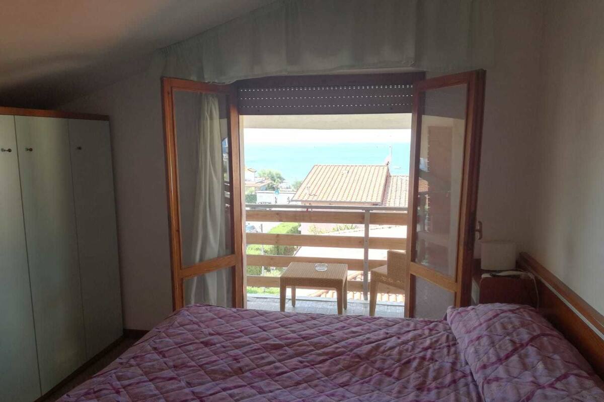 Quarto com cama, guarda-roupa e varanda com vista para o mar.