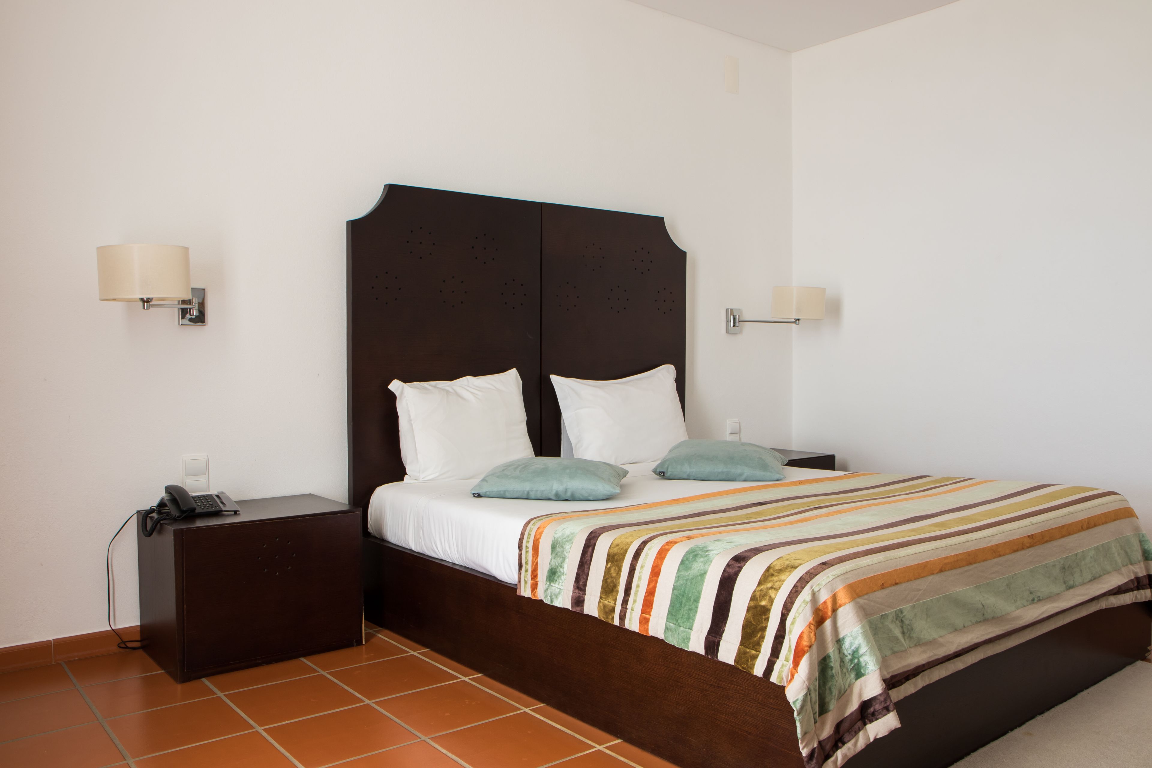 Quarto de hotel com uma cama grande, duas mesas de cabeceira e uma pequena escrivaninha com telefone.