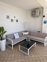 Uma sala de estar com um sofá bege, uma mesa de centro branca e uma planta em vaso.