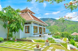 Uma casa tradicional com telhado de cerâmica, rodeada por vegetação exuberante e um cenário montanhoso.
