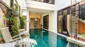 Piscina interior moderna com água cristalina, rodeada por espreguiçadeiras brancas e plantas em vasos.