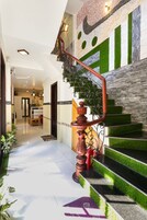 Uma escadaria moderna com degraus de grama sintética verde, corrimão de madeira e uma parede decorativa com padrões geométricos.