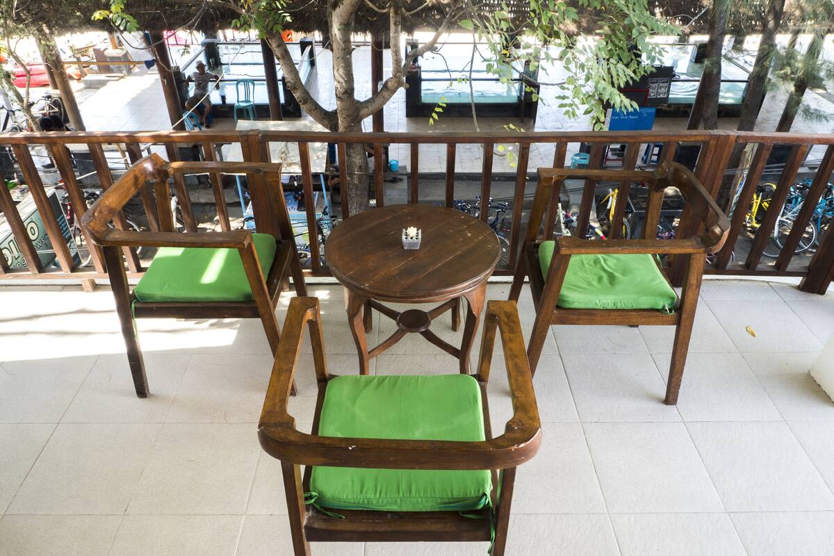 Uma área de estar ao ar livre com bancos de madeira, uma mesa redonda e cadeiras, delimitada por um guarda-corpo de madeira.