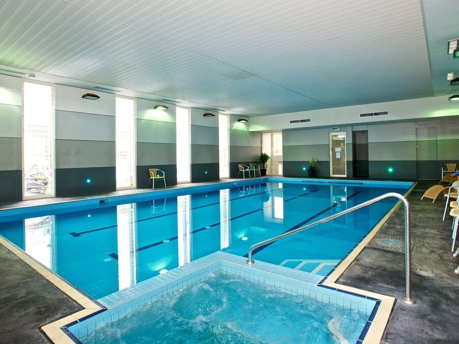 Piscina interna com pistas demarcadas, área de vestiários e espaço de descanso com cadeiras e planta em vaso.