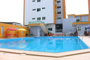 Piscina com área de estar externa e um edifício com várias andares e sacadas.