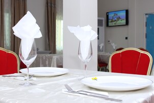 Uma mesa de jantar posta com pratos brancos, guardanapos e talheres, rodeada por cadeiras vermelhas.