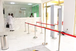 Uma área de recepção de hotel com piso de mármore, um balcão de atendimento e uma barreira de corda vermelha.