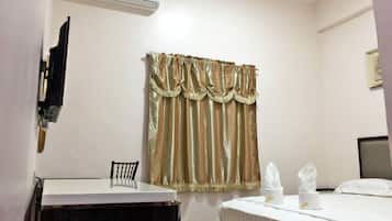 Quarto de hotel com cama, escrivaninha, cadeira, ar condicionado e janela com cortinas.