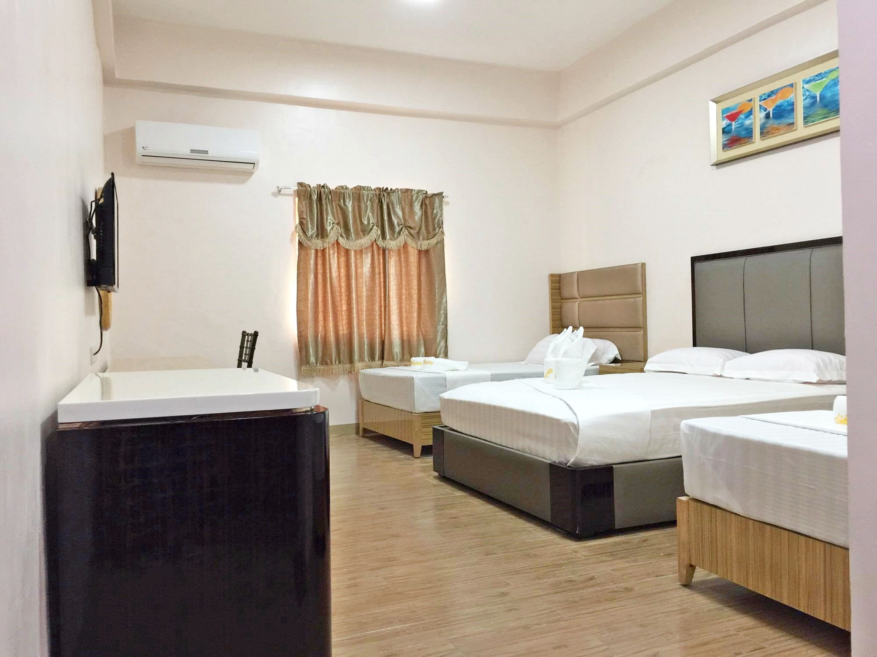 Quarto de hotel com uma cama grande, uma cama menor, uma escrivaninha com cadeira e um banheiro com pia e espelho.