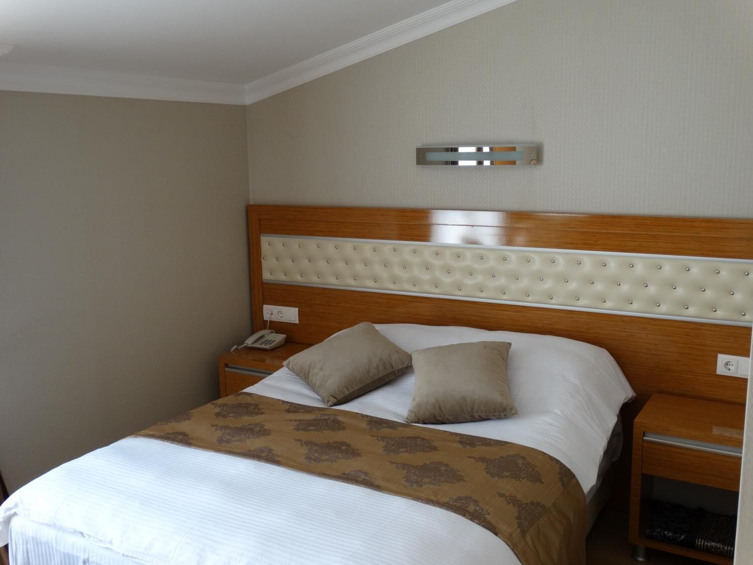 Quarto de hotel com cama, mesa de cabeceira com telefone e criado-mudo com abajur.