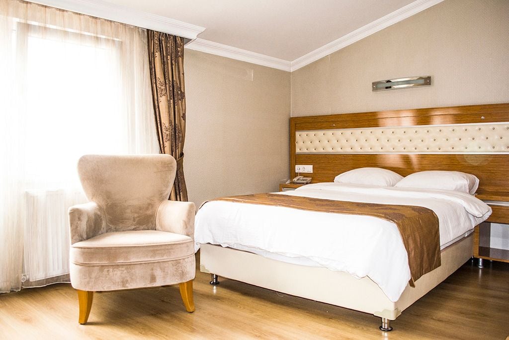 Quarto de hotel com cama, cadeira, mesa de cabeceira e janela com cortinas.