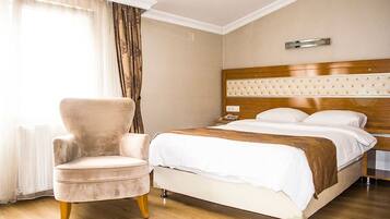 Quarto de hotel com cama, cadeira, mesa de cabeceira e janela com cortinas.