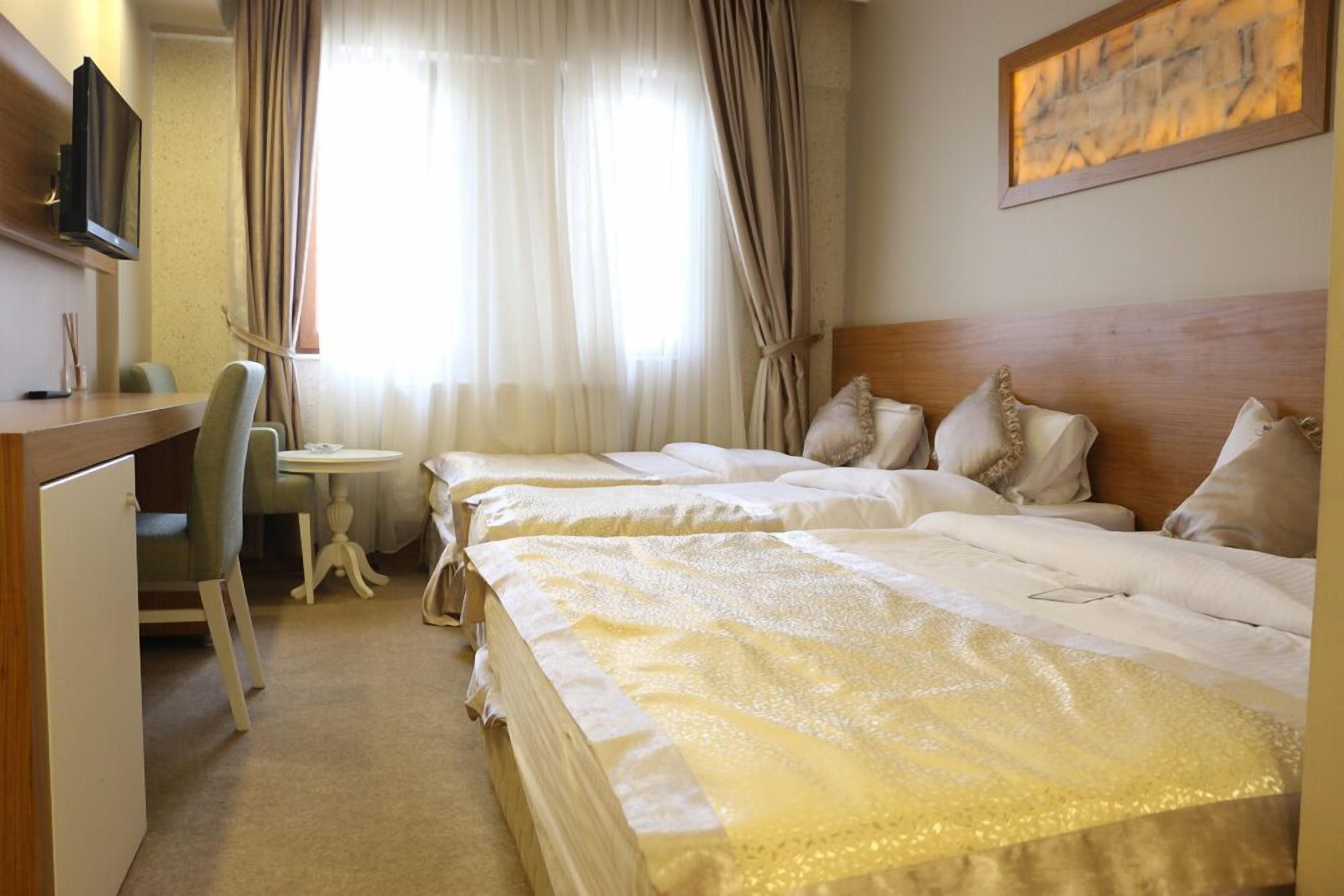 Quarto de hotel com duas camas, uma escrivaninha, uma cadeira e uma televisão.