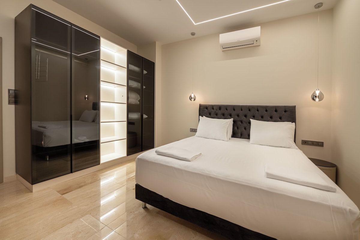 Quarto moderno com uma cama grande, um guarda-roupa com portas de correr e um lustre no teto.