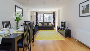 Uma sala de estar moderna com sofá, televisão e área de jantar com cadeiras e mesa.