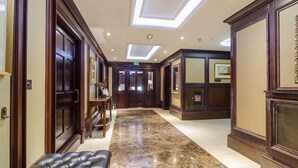 Um hall de hotel com piso de mármore, portas de madeira e um banco.
