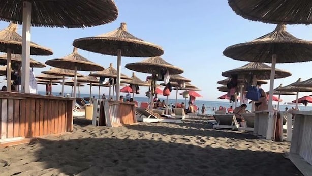 Uma praia com guarda-sóis de palha e estruturas de madeira, provavelmente para proteção solar.