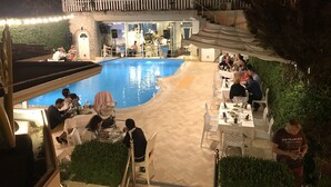 Área de piscina externa com mesas e cadeiras, cercada por um muro branco e coberta por um toldo.