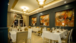Restaurante com toalhas brancas nas mesas, cadeiras douradas e grandes quadros nas paredes.