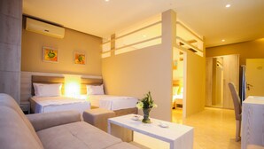 Quarto de hotel com duas camas, um sofá, uma mesa pequena e um banheiro visível por uma porta aberta.