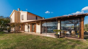 Uma casa com uma grande extensão de vidro, um pátio com móveis de exterior e um jardim.