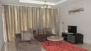 Uma sala de estar com sofá, banqueta, mesa de centro e um rack para TV.