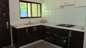 Cozinha com armários escuros, bancada branca, pia, fogão e forno.