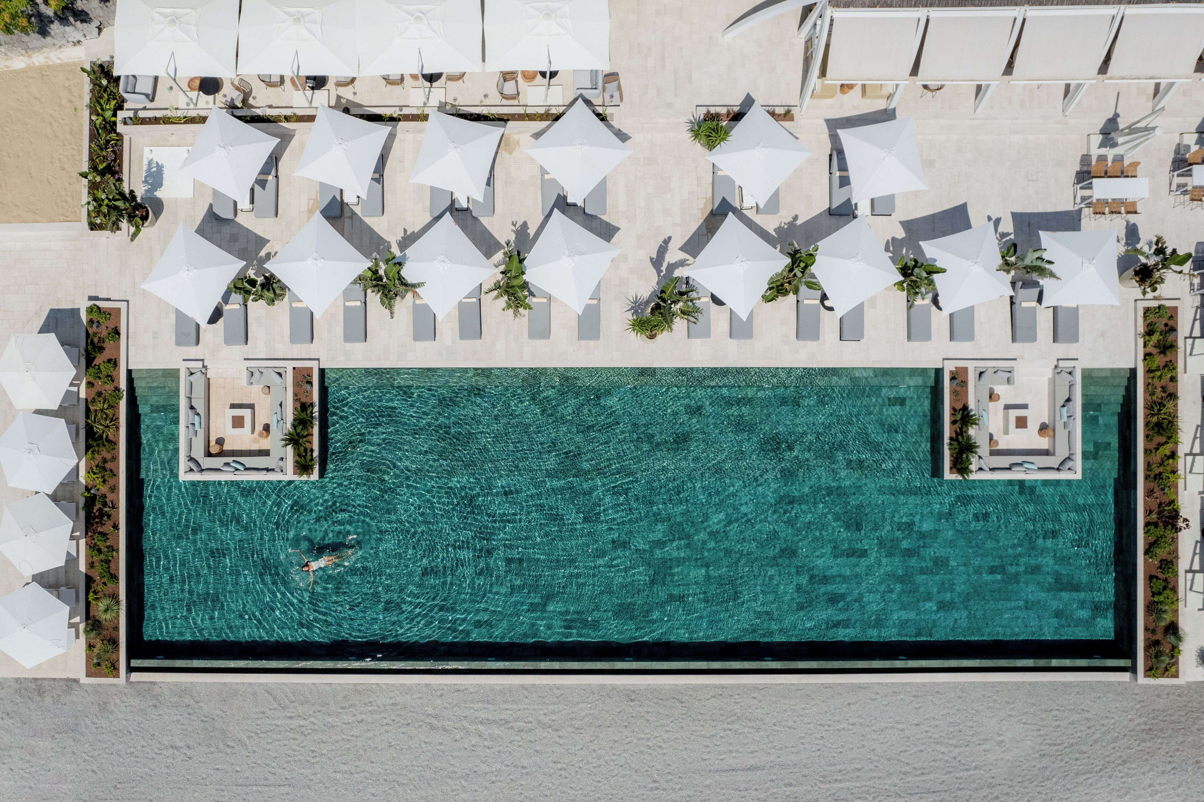 Vista aérea de um resort com piscina central, espreguiçadeiras e guarda-sóis.
