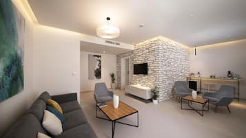 Uma sala de estar moderna com uma parede de destaque em pedra, uma TV de tela plana e uma área de estar aconchegante com um sofá e poltronas.