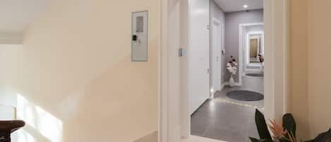 Um corredor com piso xadrez, um vaso de planta e uma porta que dá para outro cômodo.