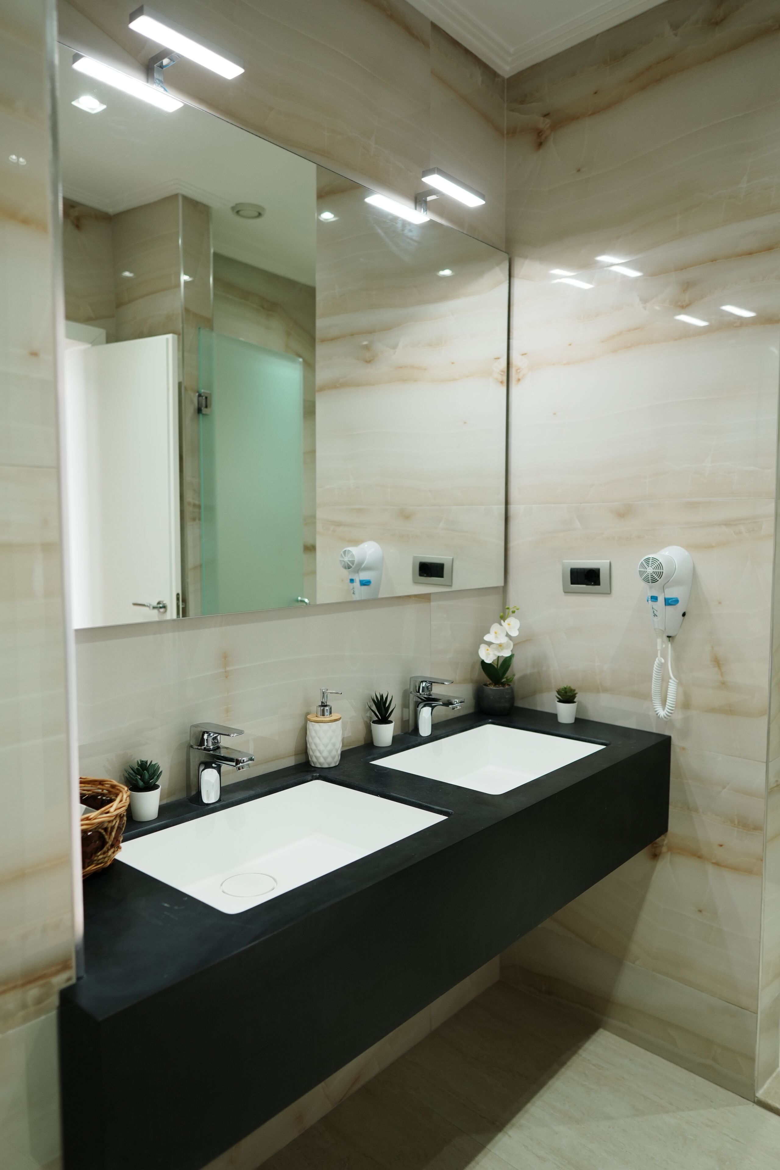 Uma casa de banho moderna com duas pias, um espelho grande e um secador de cabelo fixado na parede.