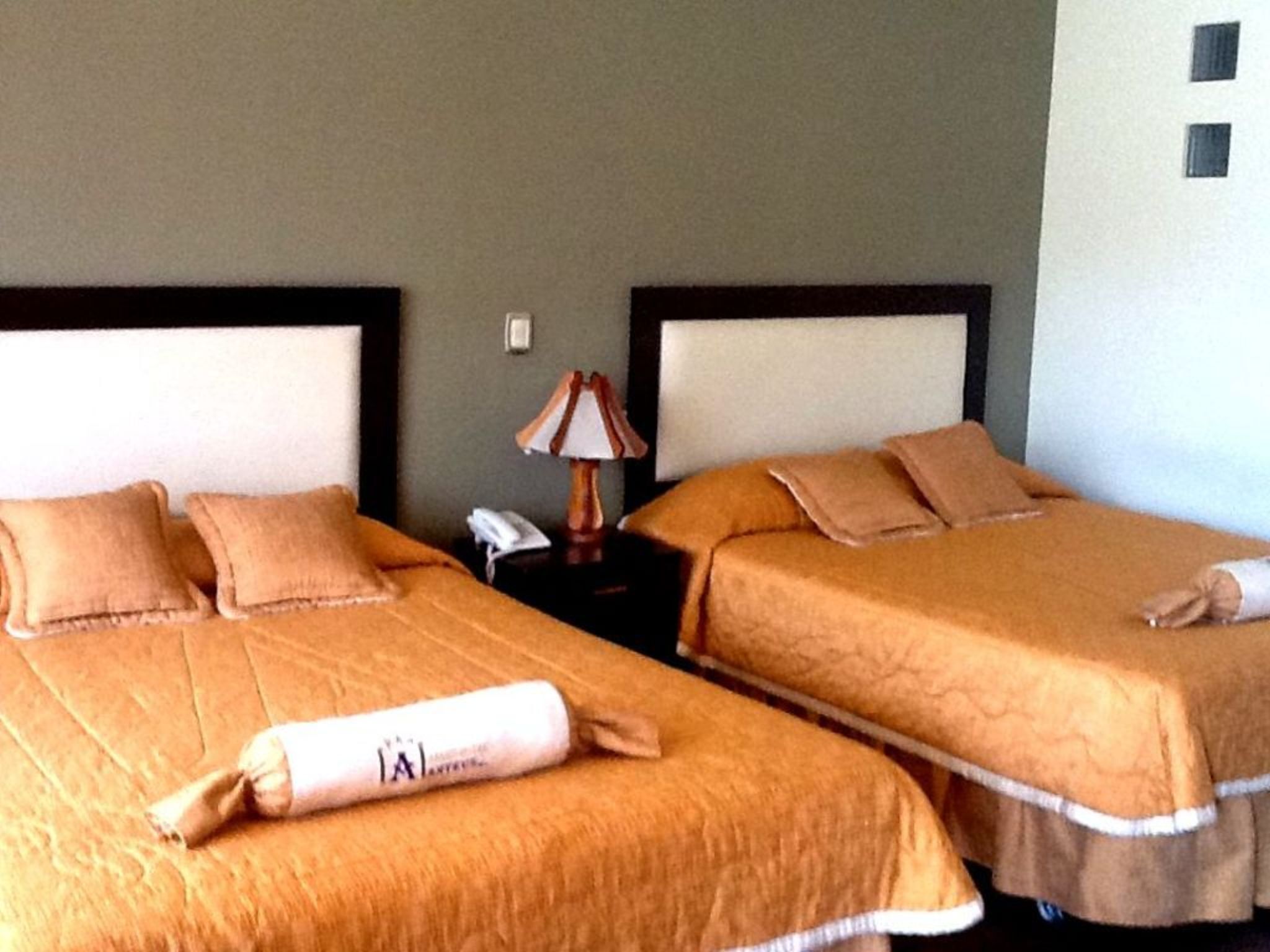 Duas camas de solteiro com cabeceiras iguais, uma mesa de cabeceira com abajur e um telefone.