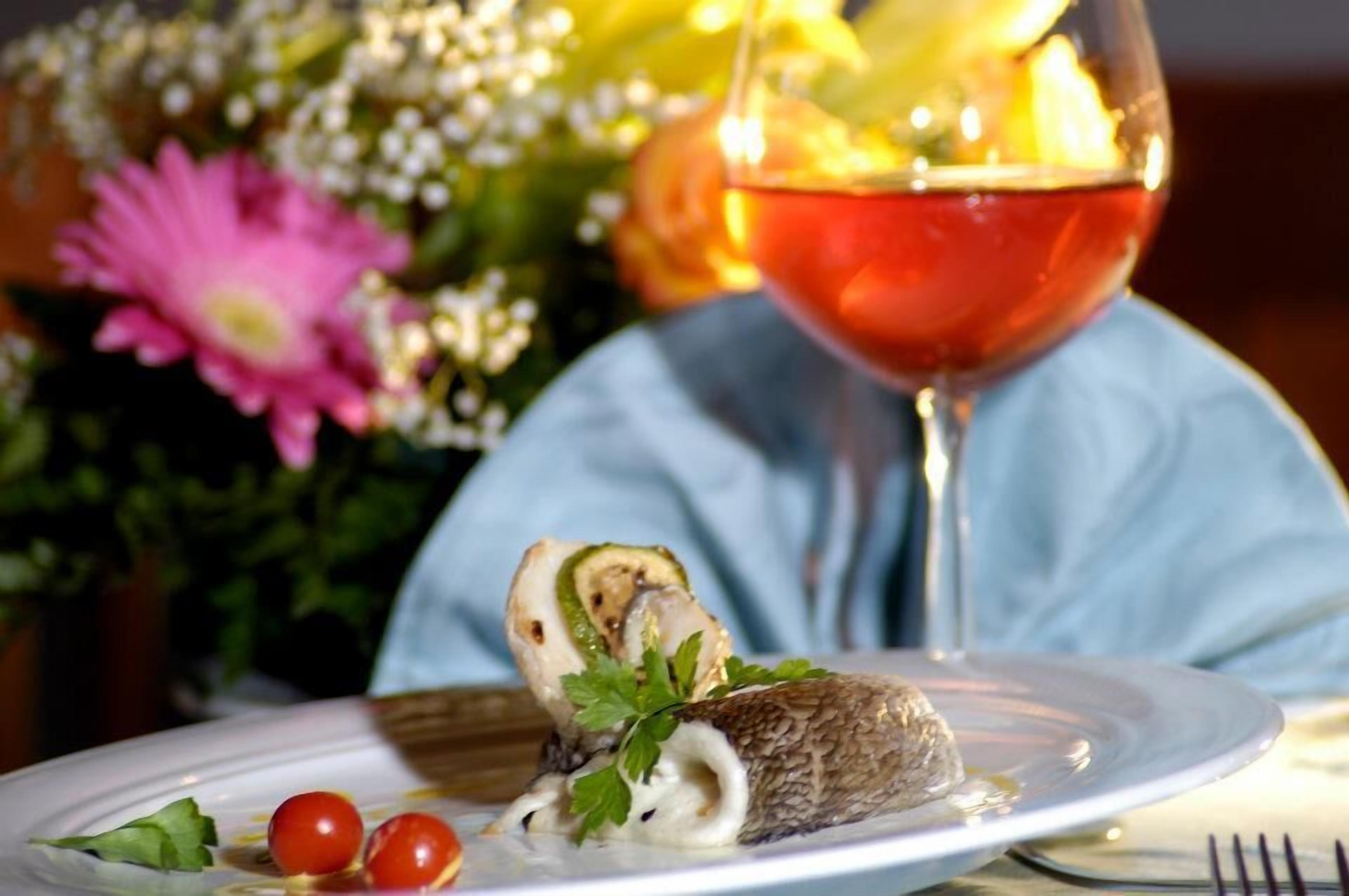 Um prato com um ensopado de peixe, um copo de vinho tinto e uma flor rosa.
