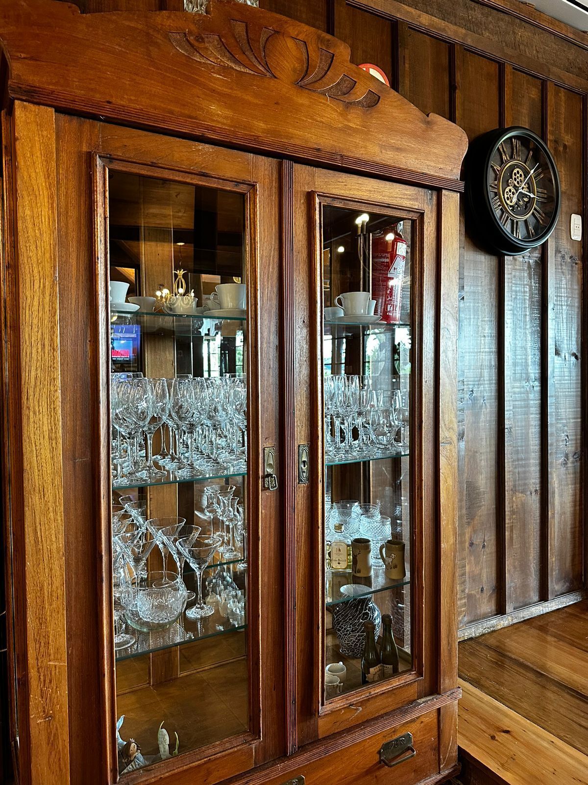 Um armário de madeira com portas de vidro exibindo diversos utensílios de cozinha e peças de vidro.