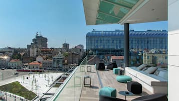 Terraço no telhado com assentos, guarda-corpo de vidro e vista para a paisagem urbana com edifícios modernos.