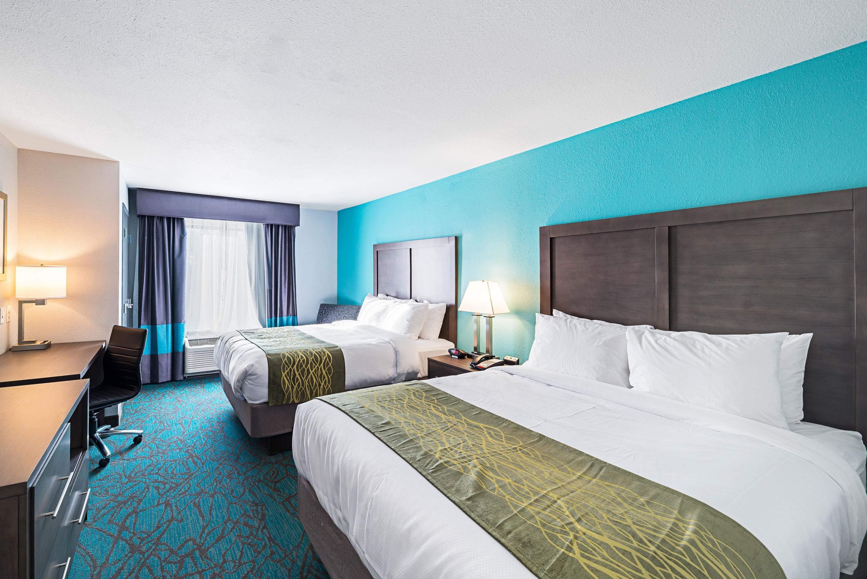 Quarto de hotel com duas camas, uma escrivaninha e uma cadeira.