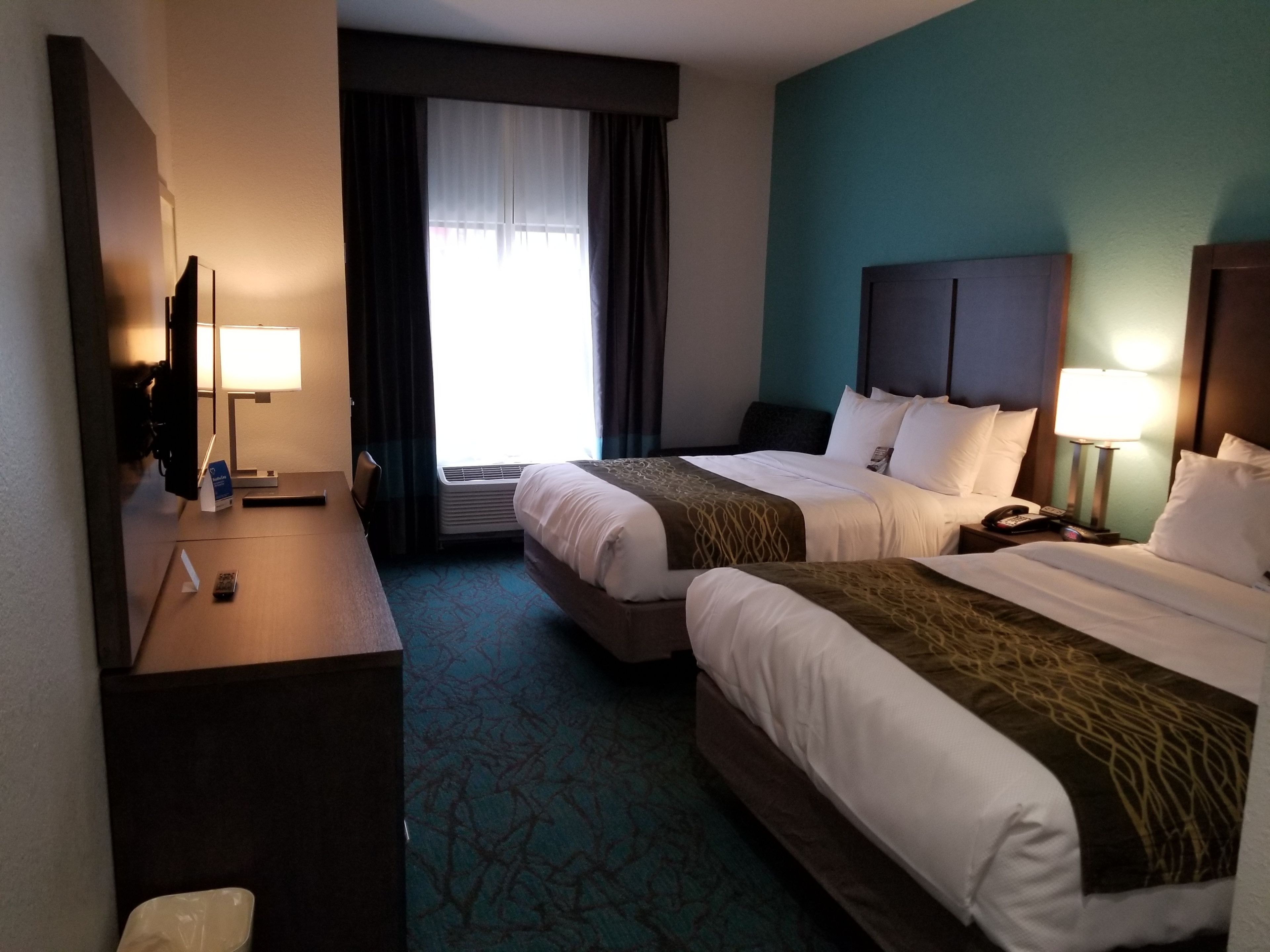 Quarto de hotel com duas camas, uma escrivaninha, uma televisão e uma janela com cortinas.