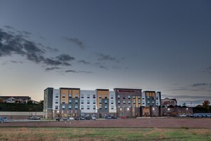 Hotel de vários andares com design moderno, com fachada em vidro e tijolo, e estacionamento em frente.