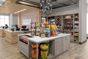 Área de recepção de hotel com balcão, computador e diversas comodidades, incluindo uma loja e máquinas de venda de lanches.