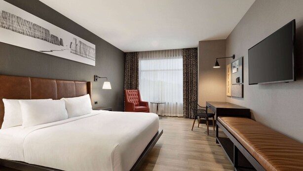 Quarto de hotel com cama grande, escrivaninha, cadeira, televisão e janela com cortinas.