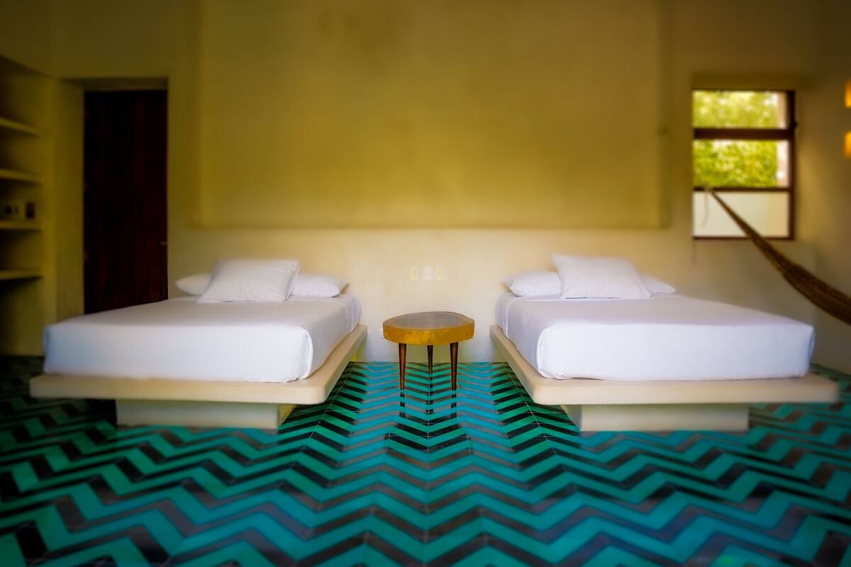 Quarto com duas camas, uma mesinha redonda e piso estampado.