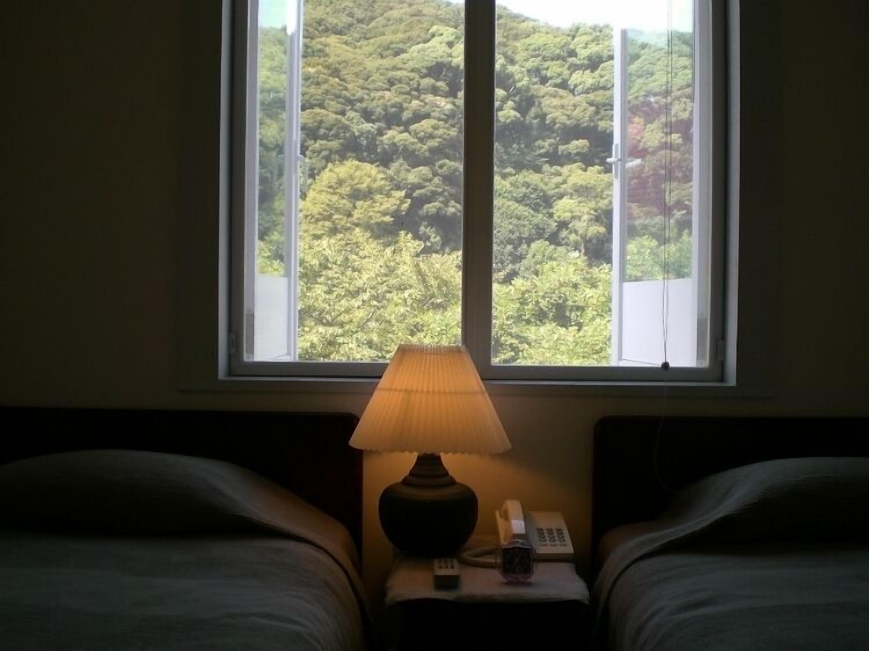 Quarto de hotel com cama, luminária, telefone e janela com vista para uma floresta.