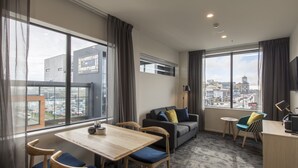 Quarto de hotel moderno com área de refeições, sofá e vista da cidade.