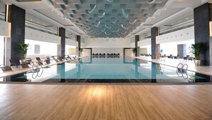 Piscina interior moderna com chão de madeira, guarda-corpos de vidro e teto com padrões geométricos.