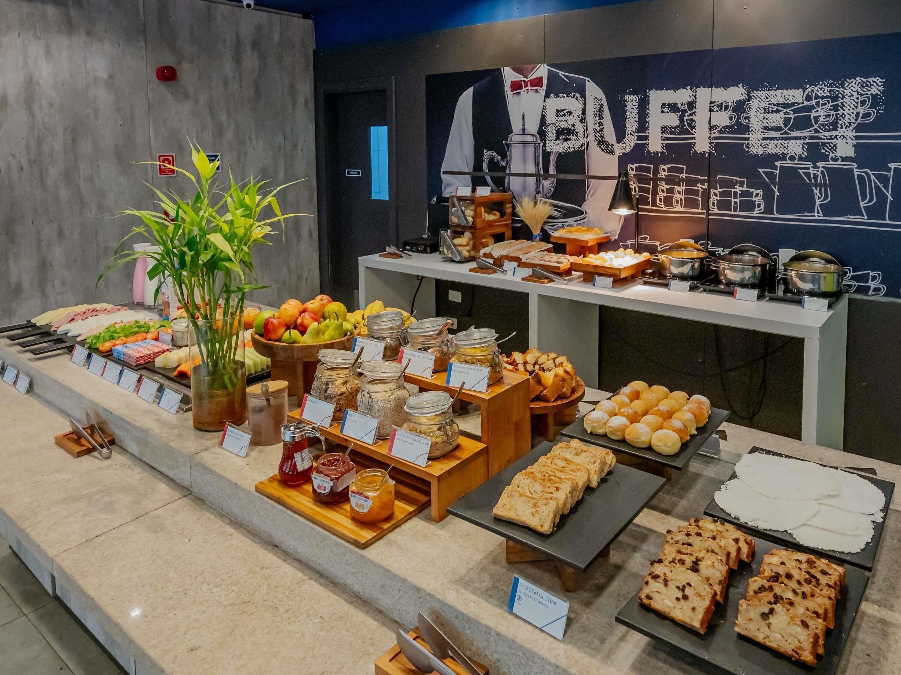 Buffet com diversas opções de comida, incluindo frutas, pães e acompanhamentos.