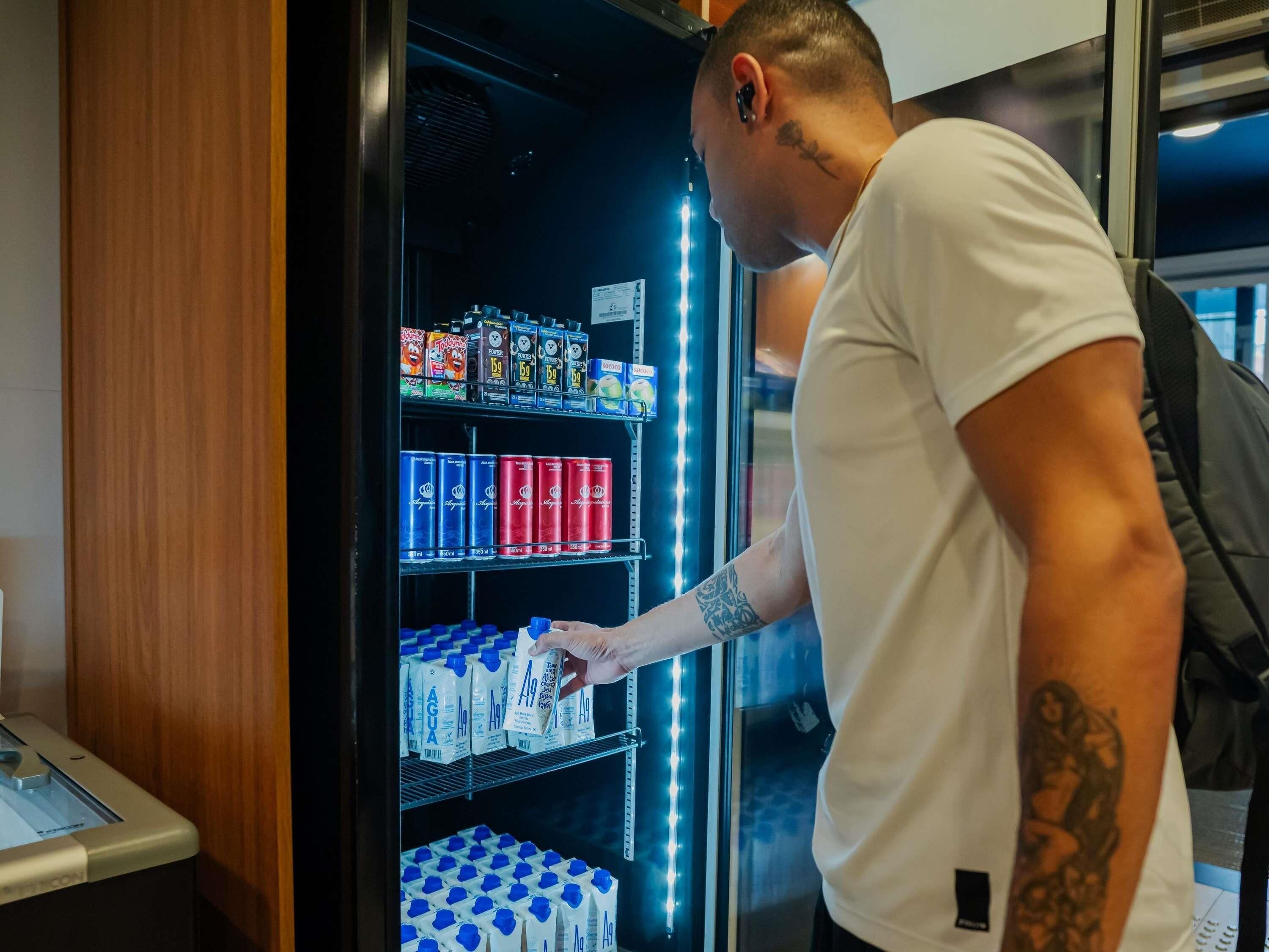 Uma pessoa interagindo com uma máquina de vendas automática recheada de bebidas e petiscos.