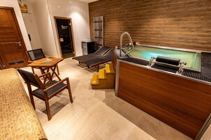 Uma área de spa com parede de madeira, banheira de hidromassagem, cadeiras de descanso e uma pequena mesa com um laptop.
