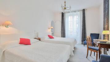 Quarto de hotel com duas camas, uma escrivaninha, uma cadeira e um candelabro.