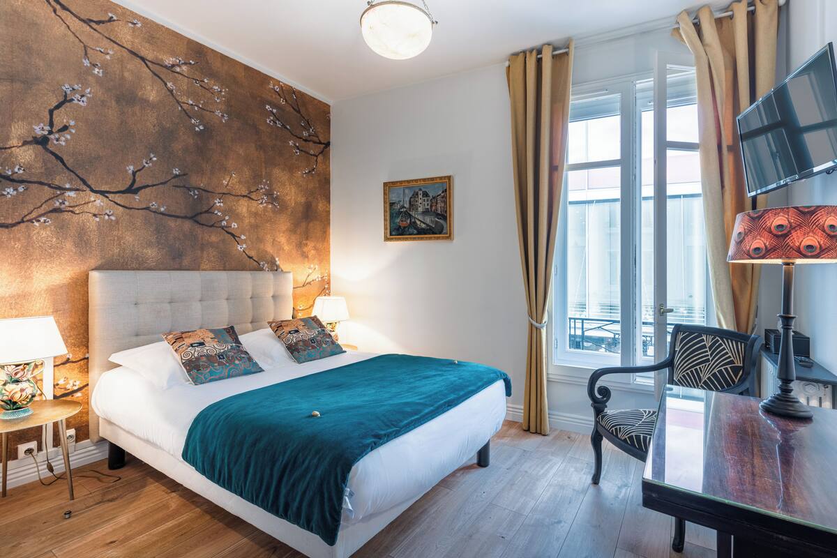 Quarto de hotel com cama, quadro, televisão, mesa e cadeira.