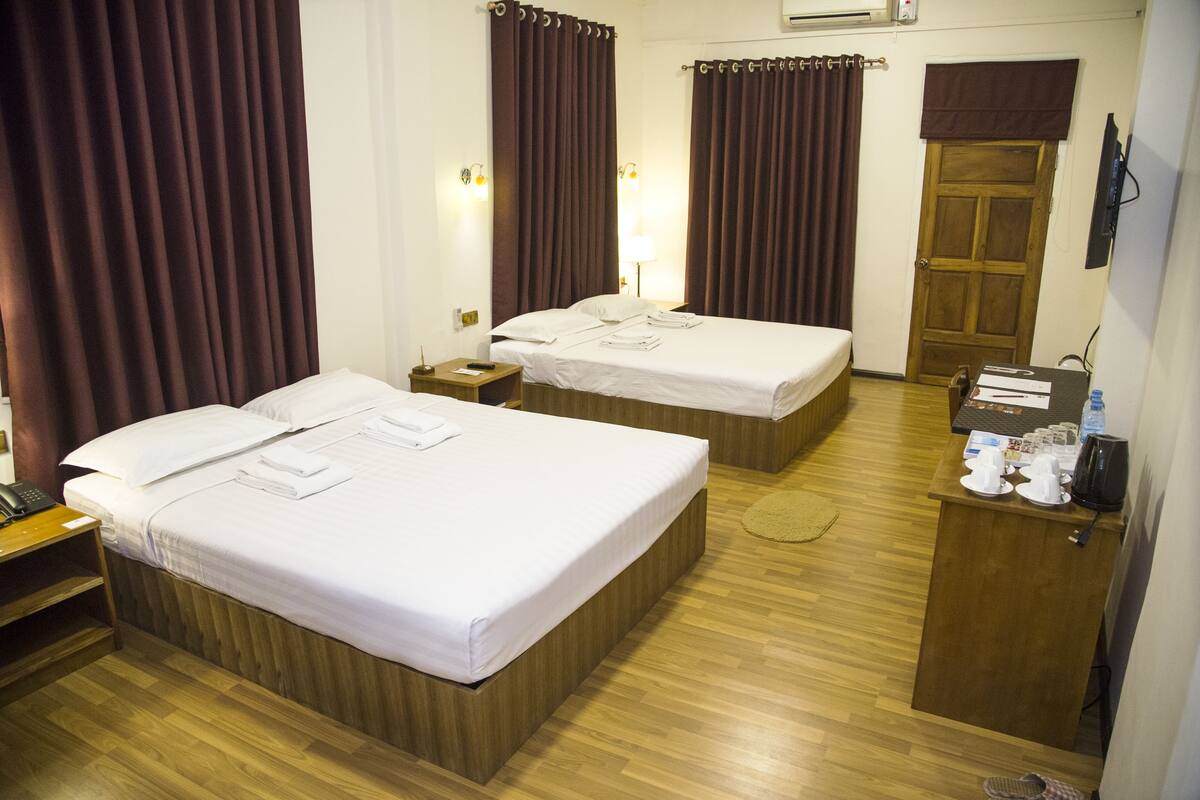 Quarto de hotel com duas camas de solteiro, piso de madeira, escrivaninha com telefone e um pequeno espaço para sentar.